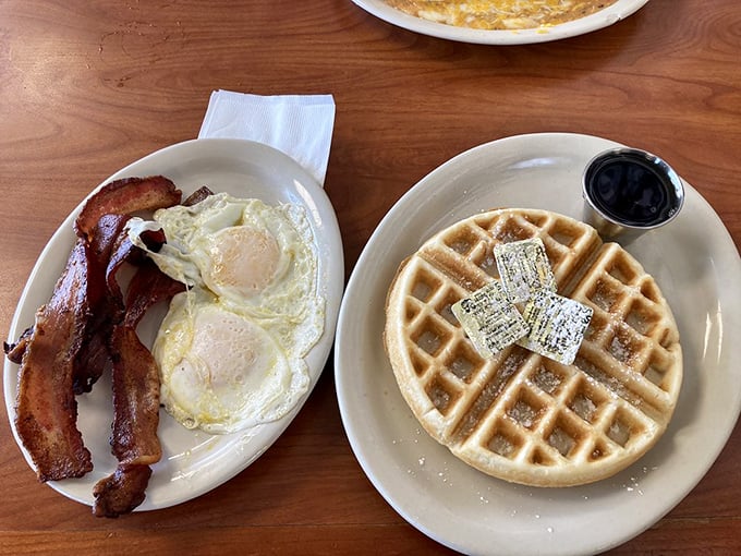 Breakfast's perfect trinity: golden waffle, crispy bacon, and sunny-side-up eggs—a holy alliance of morning deliciousness.