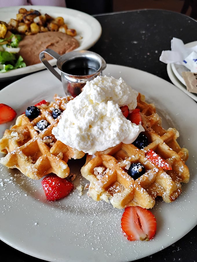Waffles that deserve their own ZIP code, crowned with fresh berries and whipped cream that's practically floating. Breakfast royalty has arrived.