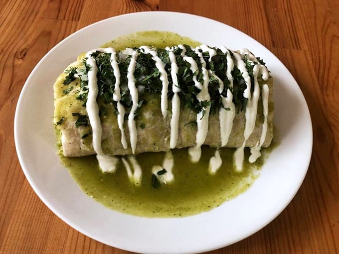 The green chili burrito in all its glory &ndash; bathed in vibrant sauce and adorned with perfect stripes of sour cream. Food architecture at its finest.