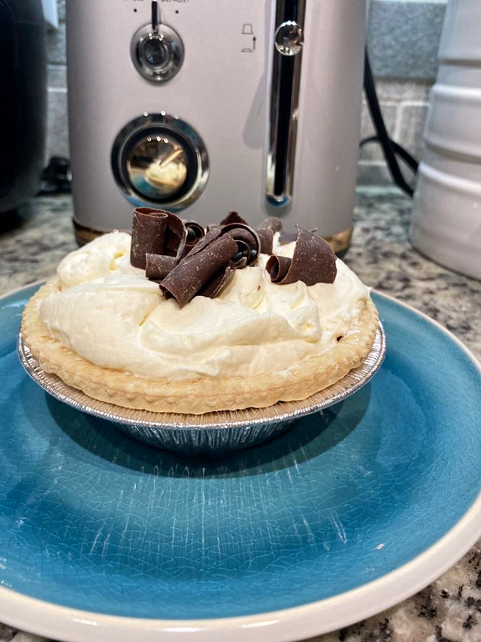 Chocolate cream pie with chocolate curls that look like they're auditioning for a dessert magazine cover. The filling appears darker than my coffee and twice as addictive.
