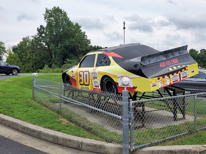 Every proper raceway needs its aspirational centerpiece. This stock car sits like a yellow-jacketed bouncer, reminding visitors what real speed looks like.