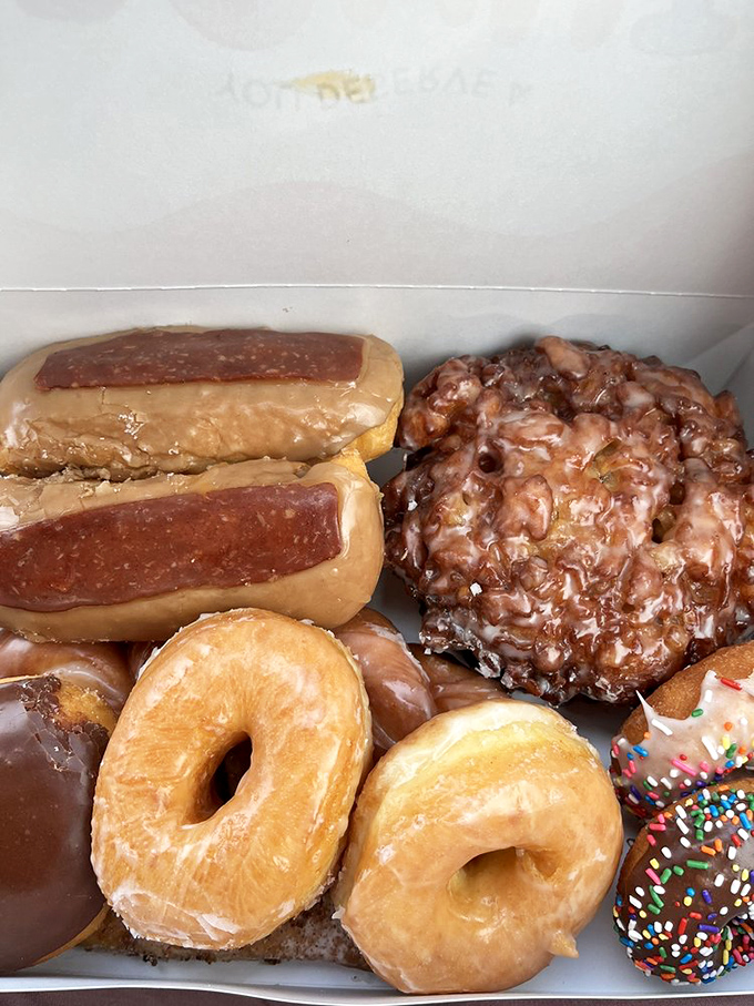 Donut nirvana in a white box – featuring maple bars that would make Canadians weep with joy and an apple fritter that deserves its own ZIP code.