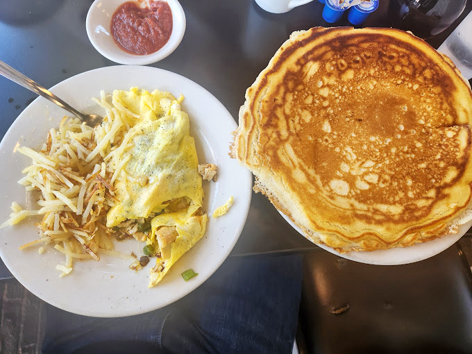 Breakfast perfection on a plate: a golden omelet nestled beside crispy hash browns with a pancake standing by like a delicious backup singer.