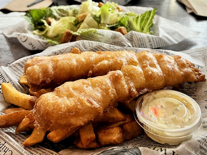 Golden-battered fish resting on a bed of thick-cut chips. This isn't just fried food&mdash;it's edible sunshine wrapped in newspaper.