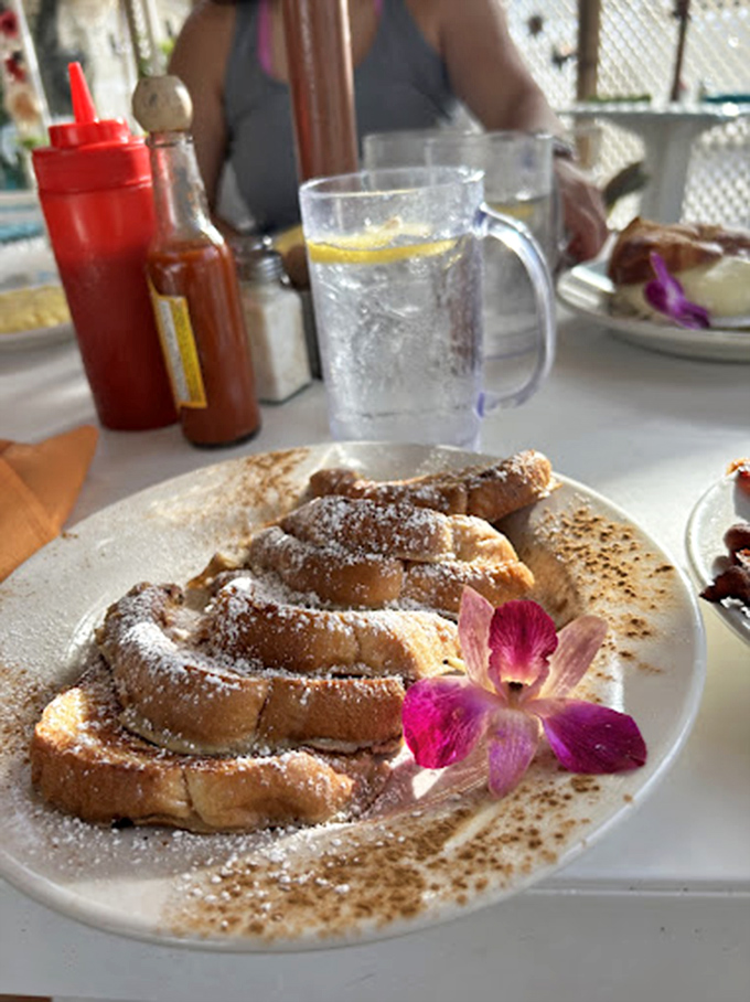 This French toast doesn't just arrive at your table—it makes an entrance, dusted with powdered sugar and adorned with an orchid like it's headed to a tropical gala.
