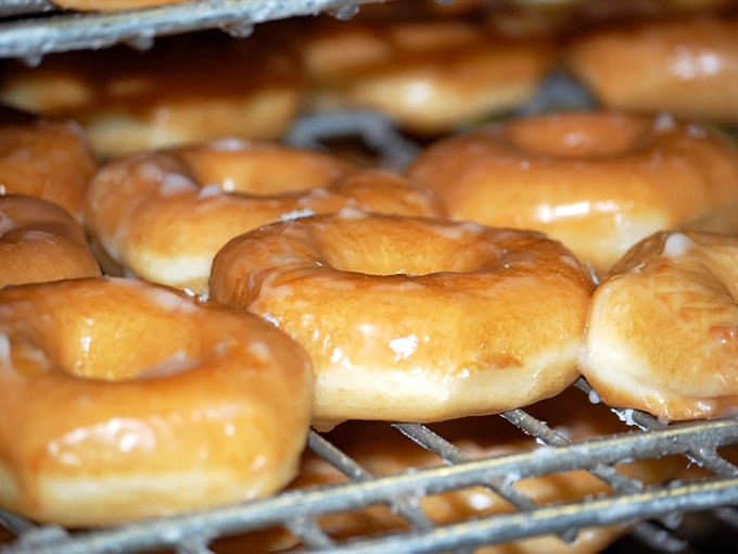 Fresh glazed beauties cooling on the rack, their glistening tops catching the light like sugary stained glass. This is what donut dreams are made of.