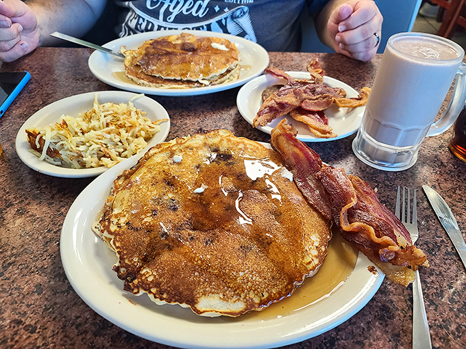 Pancakes shouldn't wear tuxedos. These golden discs of joy arrive exactly as God intended—bigger than the plate and flanked by bacon that means business.