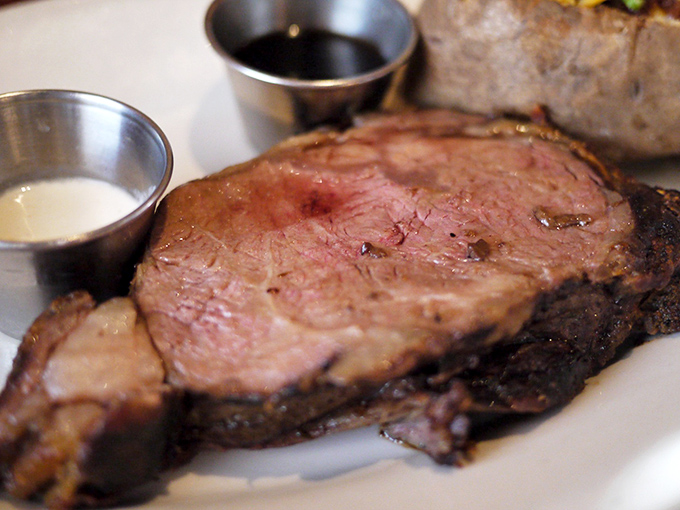 Prime rib perfection that makes vegetarians question their life choices—perfectly pink, accompanied by those essential silver cups of jus and horseradish.