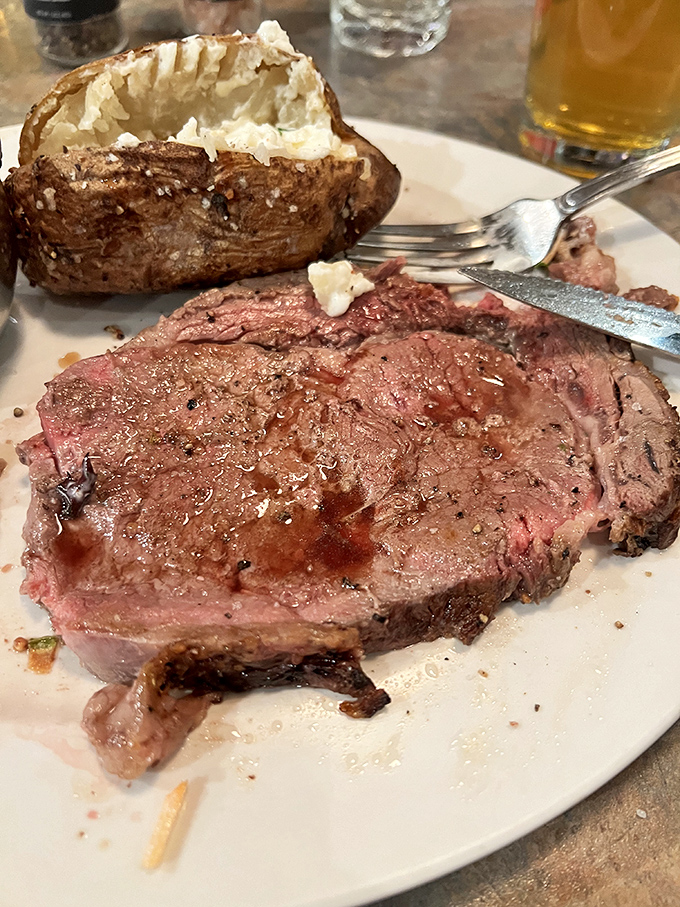 Behold the star attraction! A perfectly pink prime rib alongside a baked potato bursting with fluffy goodness &ndash; carnivore nirvana achieved on a simple white plate.