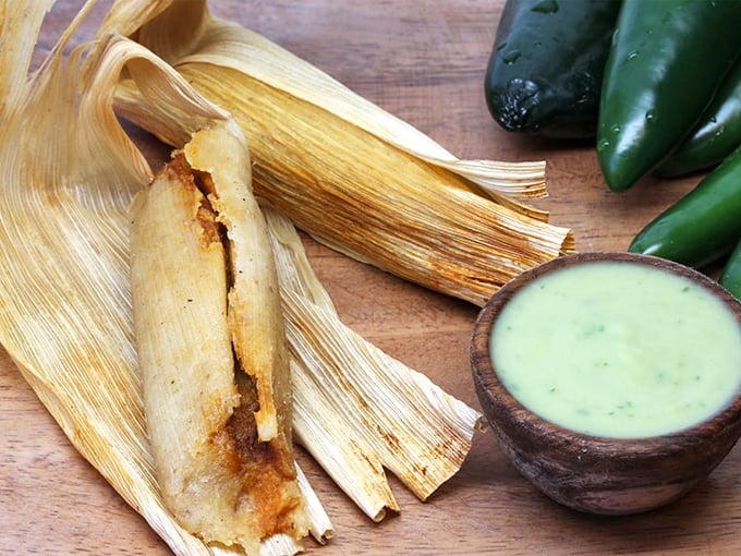 Behold the humble tamale in its natural habitat &ndash; corn husk opened to reveal its treasures, with that green sauce standing by like a faithful companion.