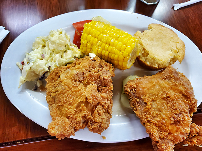 A plate of Southern dreams: crispy fried chicken, creamy potato salad, sweet corn, and cornbread that could make your grandmother jealous.