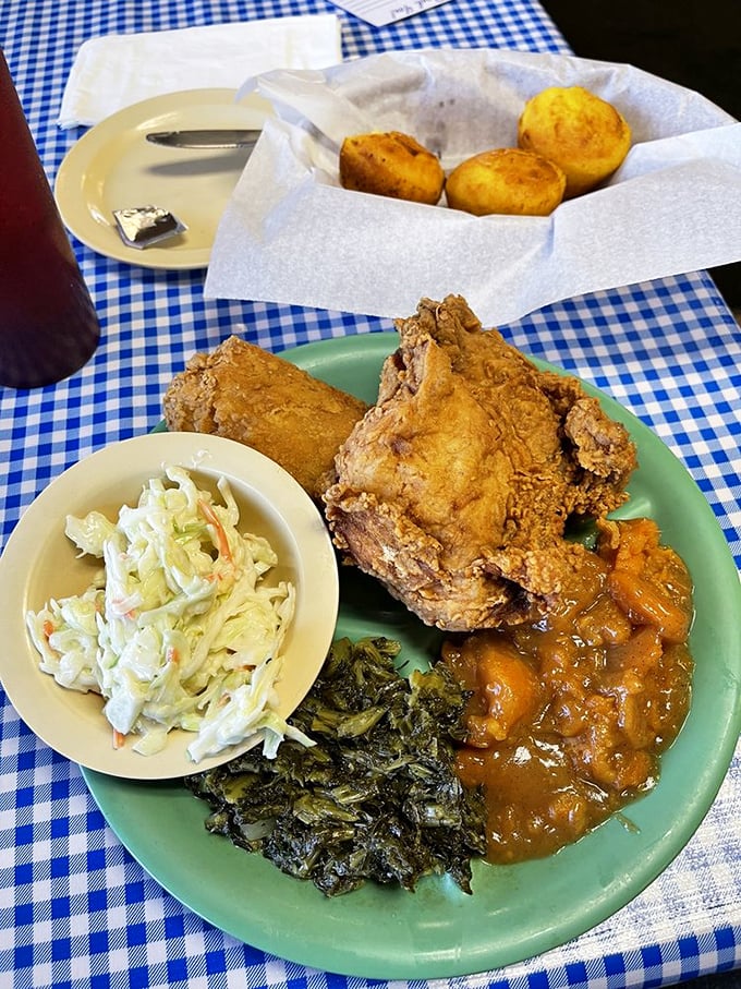 Cornbread drowning in gravy, collard greens, and fried chicken&mdash;the holy trinity of Southern cuisine on a turquoise plate.