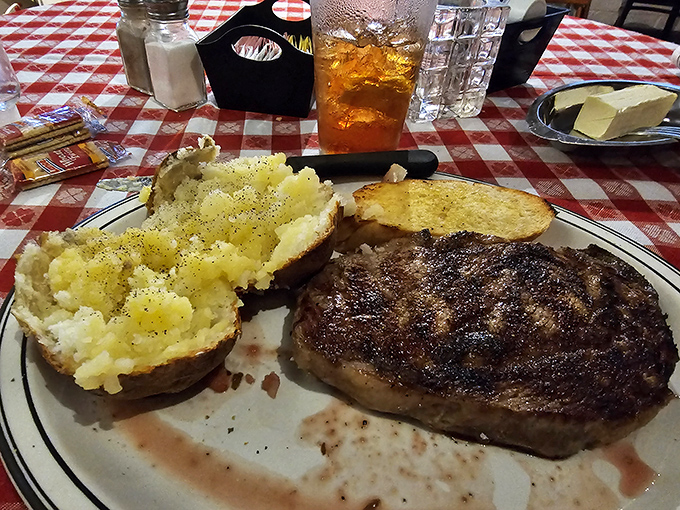 The holy trinity of steakhouse perfection: charred ribeye, fluffy baked potato, and that essential grilled bread.