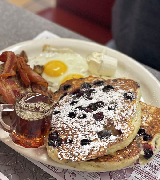 Blueberry pancakes dusted with powdered sugar alongside perfectly cooked eggs and bacon—the breakfast trinity that makes mornings worth facing.