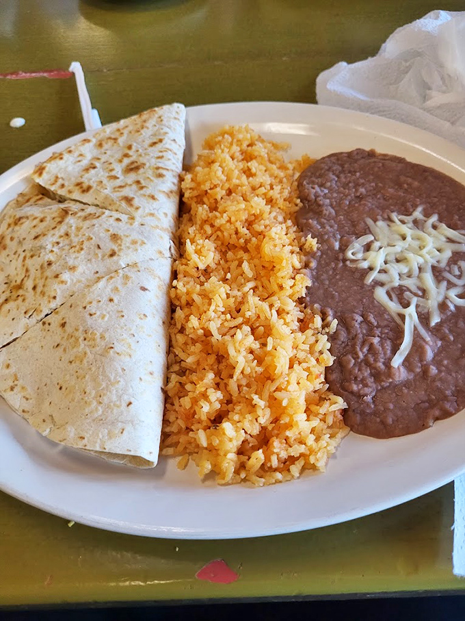 The holy trinity of Mexican comfort food: golden quesadilla, sunset-orange rice, and refried beans topped with cheese that melts like your resistance to ordering dessert.