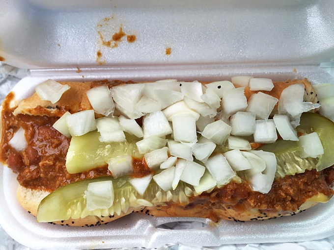 Diced onions scattered across this chili dog like confetti at a parade. The pickle spear stands guard, ensuring every bite delivers the perfect crunch-to-squish ratio.