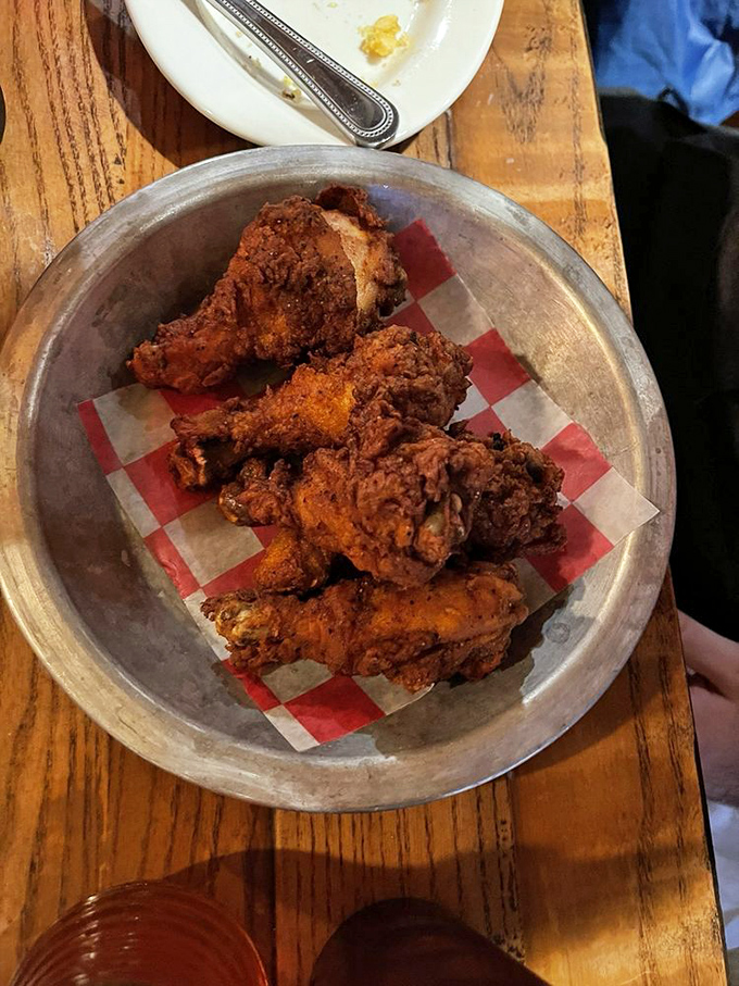 A metal tray cradles these crispy drumsticks like the culinary treasures they are. The red-checkered paper is basically a welcome mat for your taste buds.