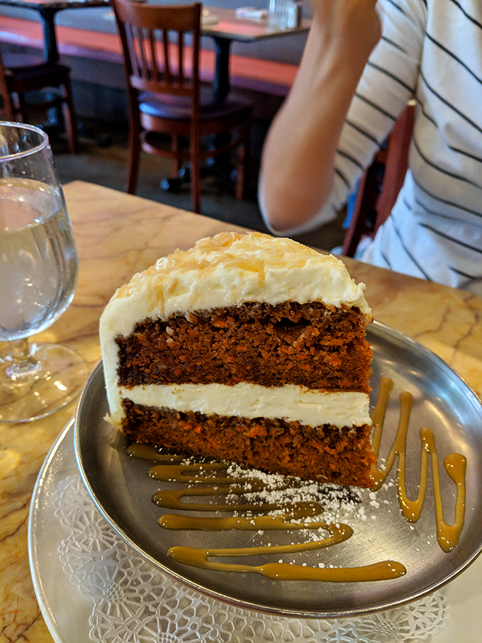 Two perfect layers of moist carrot cake embrace cream cheese frosting like long-lost lovers, all drizzled with caramel that's practically serenading the plate.