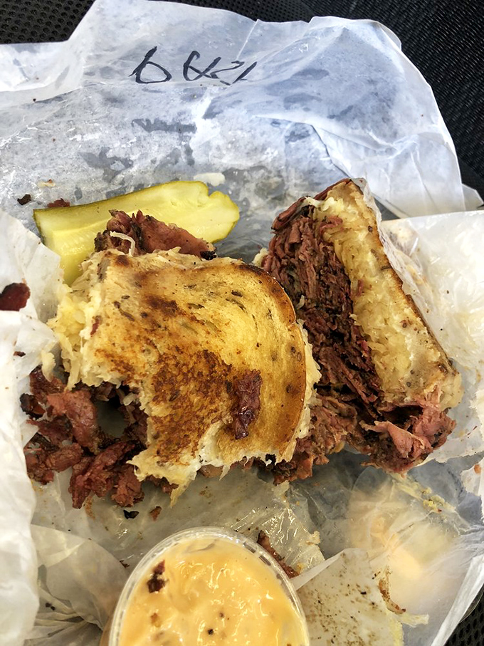 The Reuben in its natural habitat: wrapped in deli paper, oozing with cheese, accompanied by a pickle sentinel standing guard. Poetry on wax paper.