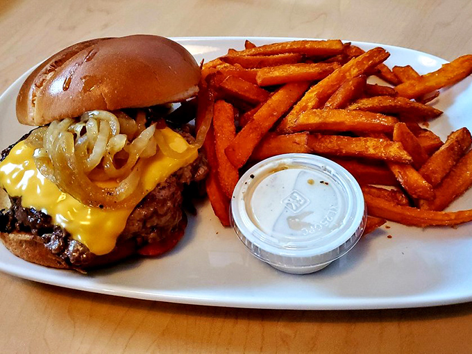 Melted cheese cascades down this burger's sides like a yellow waterfall of deliciousness, while sweet potato fries stand at attention nearby.