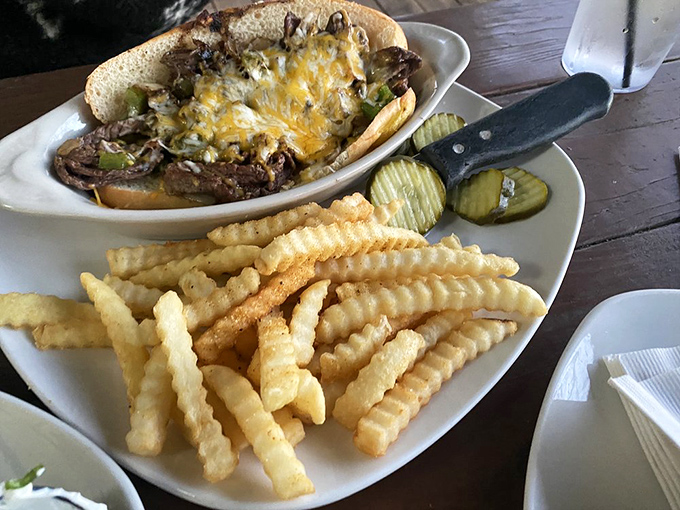 The Philly cheese steak arrives like a delicious time capsule, complete with perfectly crisp crinkle-cut fries and pickles standing guard on the side.
