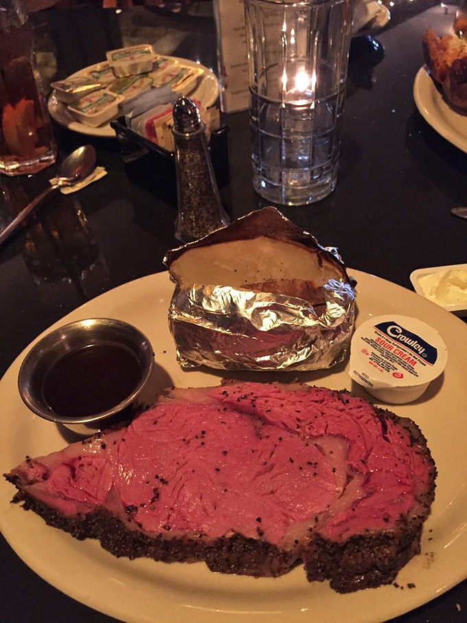 Prime rib so perfectly pink it belongs in a museum of culinary achievements, accompanied by a humble potato wearing its finest aluminum formal wear.