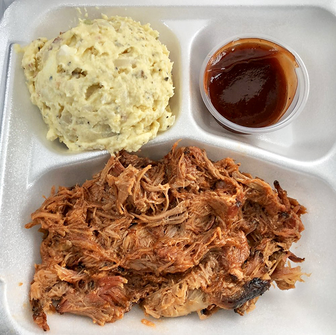 The holy trinity: pulled pork, potato salad, and sauce. A plate that proves heaven exists and it smells like hickory smoke.