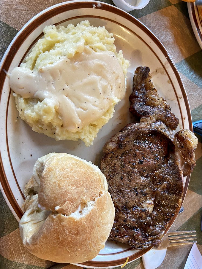The holy trinity of comfort: a juicy ribeye, cloud-like mashed potatoes with gravy, and a fresh-baked roll. Naptime may follow.