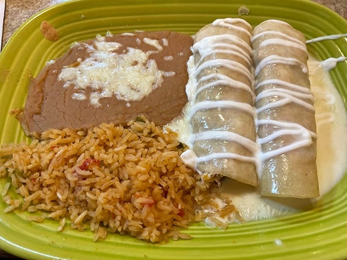 The holy trinity of Mexican dining: perfectly seasoned rice, velvety refried beans, and enchiladas draped in sauce like they're wearing their Sunday best.