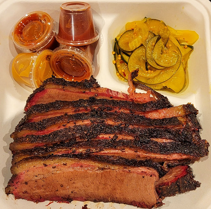 Barbecue plating at its most honest: glorious slices of brisket with that telltale smoke ring, pickles for contrast, and sauce cups standing by if needed.