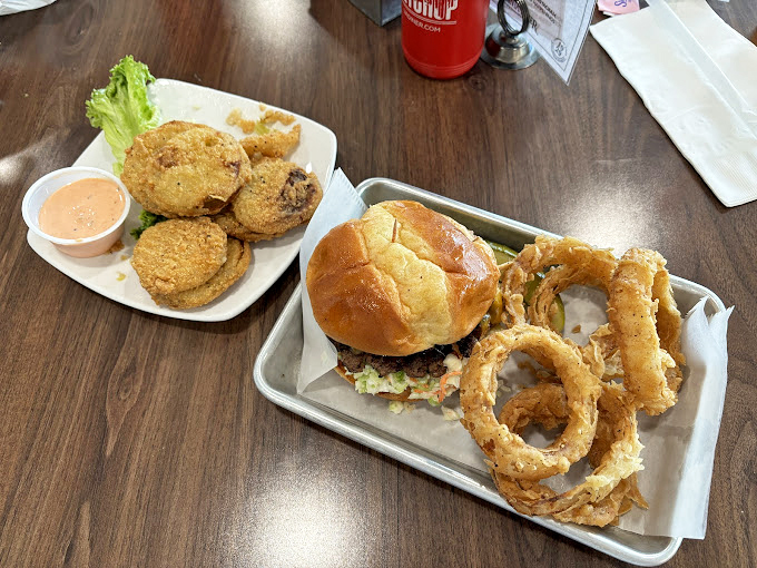 A burger that demands two hands and no distractions, paired with onion rings so perfectly golden they deserve their own Instagram account.