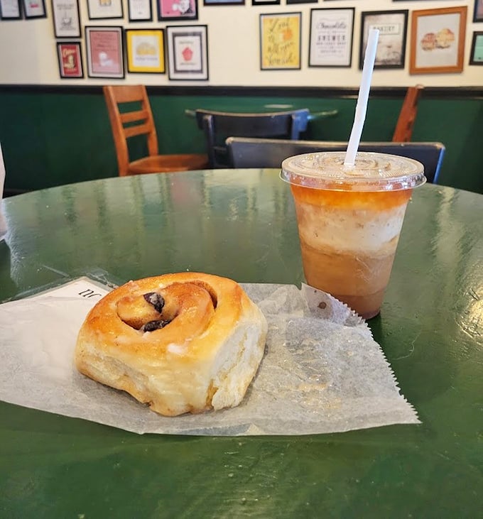 The classic pairing that dreams are made of: a hand-rolled cinnamon bun and iced coffee on a green tabletop altar of indulgence.