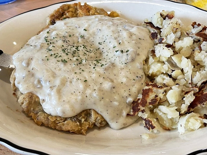 Comfort food architecture at its finest &ndash; a foundation of crispy-breaded steak supporting that perfect gravy dome, with golden hash browns standing guard on the perimeter. 
