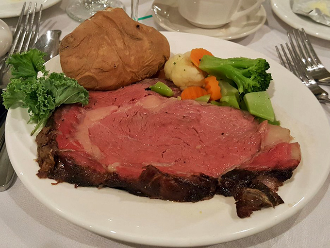 The holy trinity of steakhouse perfection: prime rib cooked to rosy magnificence, a baked potato waiting for its butter bath, and vegetables for that token nod to nutrition.