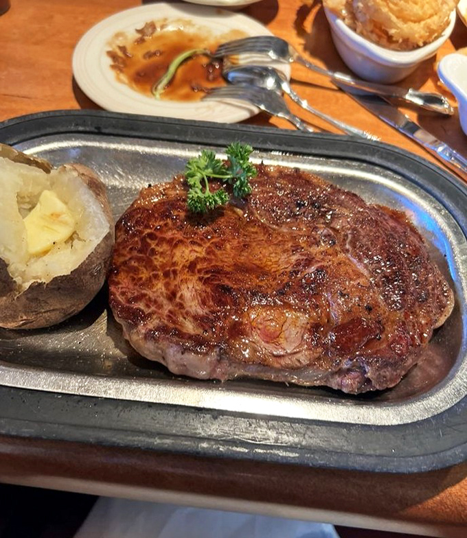 A perfectly seared ribeye rests beside a baked potato so fluffy it could double as a pillow if you fall into a meat coma.