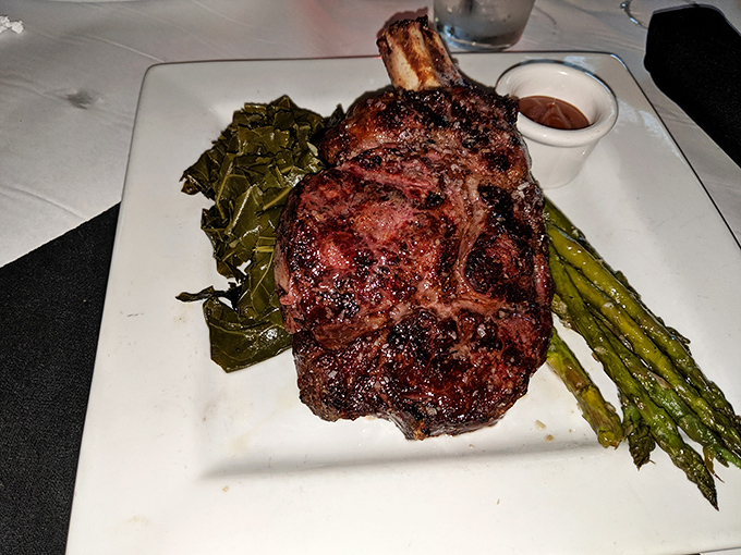 Behold the bone-in ribeye in its natural habitat—perfectly charred exterior, surrounded by collard greens and asparagus that actually deserve to share the plate.