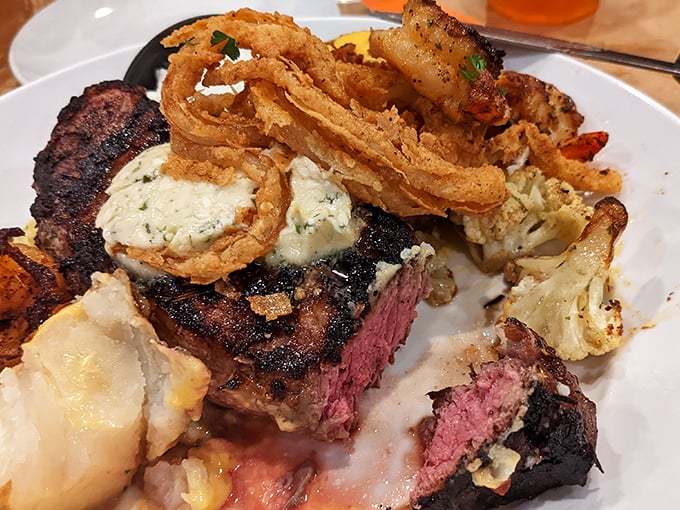 This magnificent steak, adorned with compound butter and crispy onion rings, showcases the kind of plate-filling generosity that would make your cardiologist wince and your taste buds applaud.