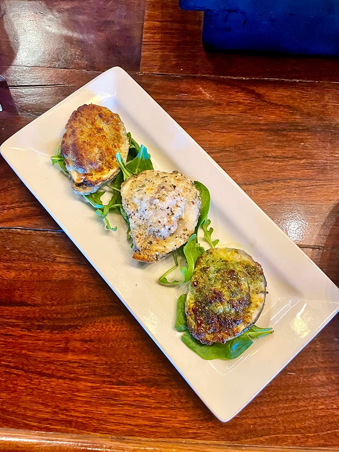A trio of baked oysters on a wooden table&mdash;like three tenors, each singing a different delicious aria on your taste buds.