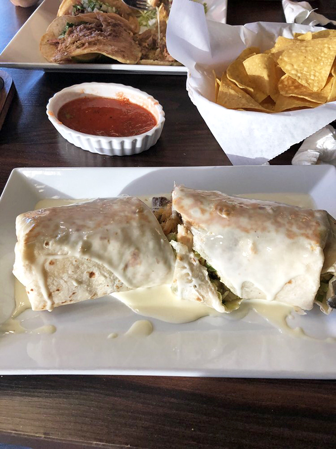 Two burritos sharing a plate like old friends catching up&mdash;one smothered in queso that cascades down the sides with magnificent abandon.