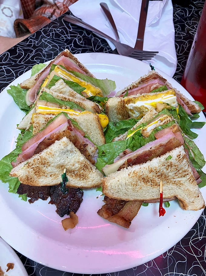 The club sandwich stands tall and proud, a skyscraper of flavor requiring both hands and possibly an engineering degree to consume properly.