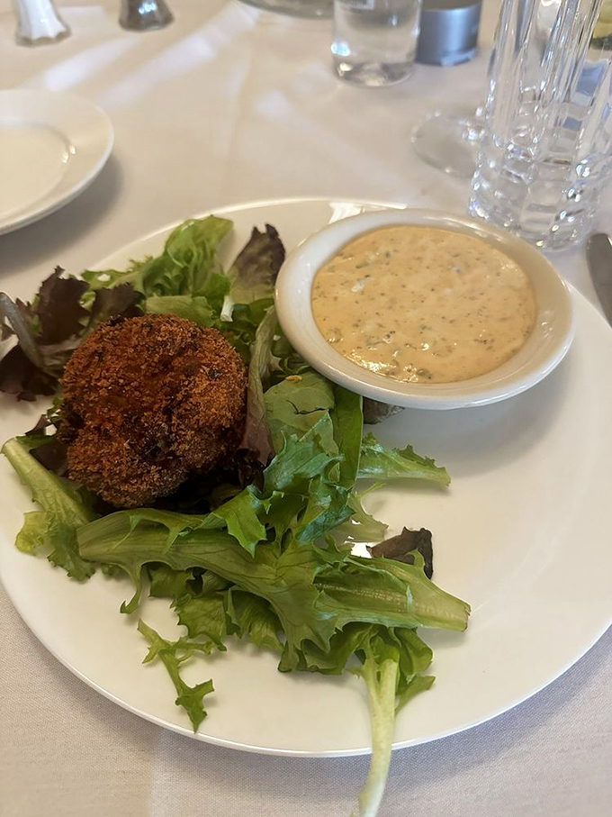 The crab cake sits regally on fresh greens, not apologizing for its golden-brown perfection. That remoulade sauce? Your new best friend.