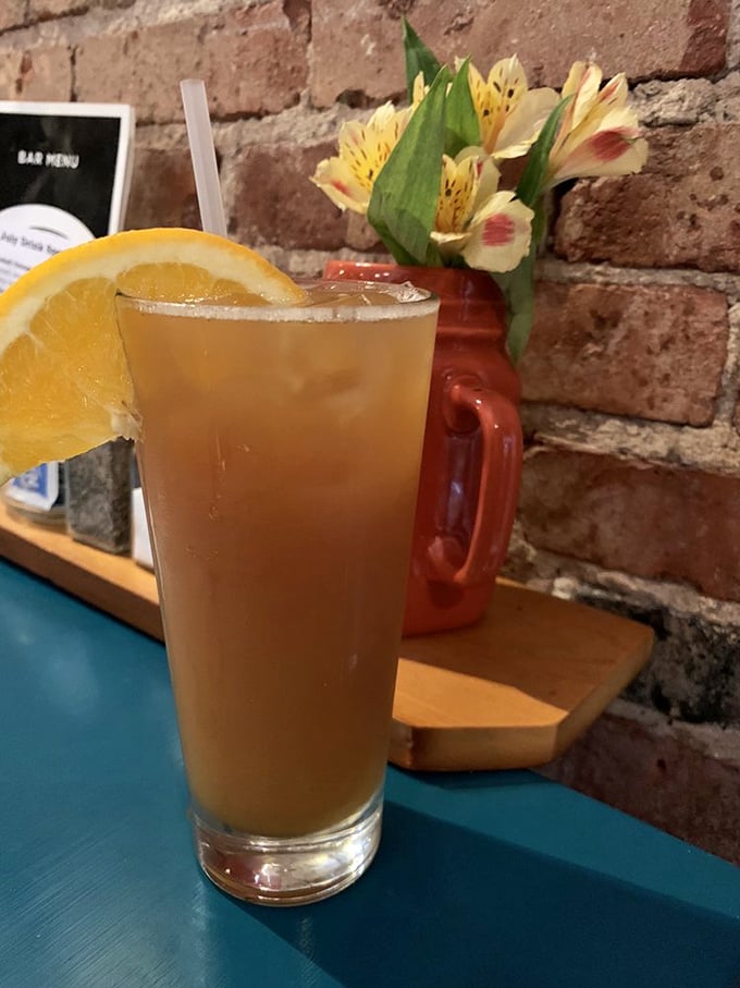A cocktail that captures Kansas sunshine in liquid form, garnished with fresh orange and served against that rustic brick backdrop.