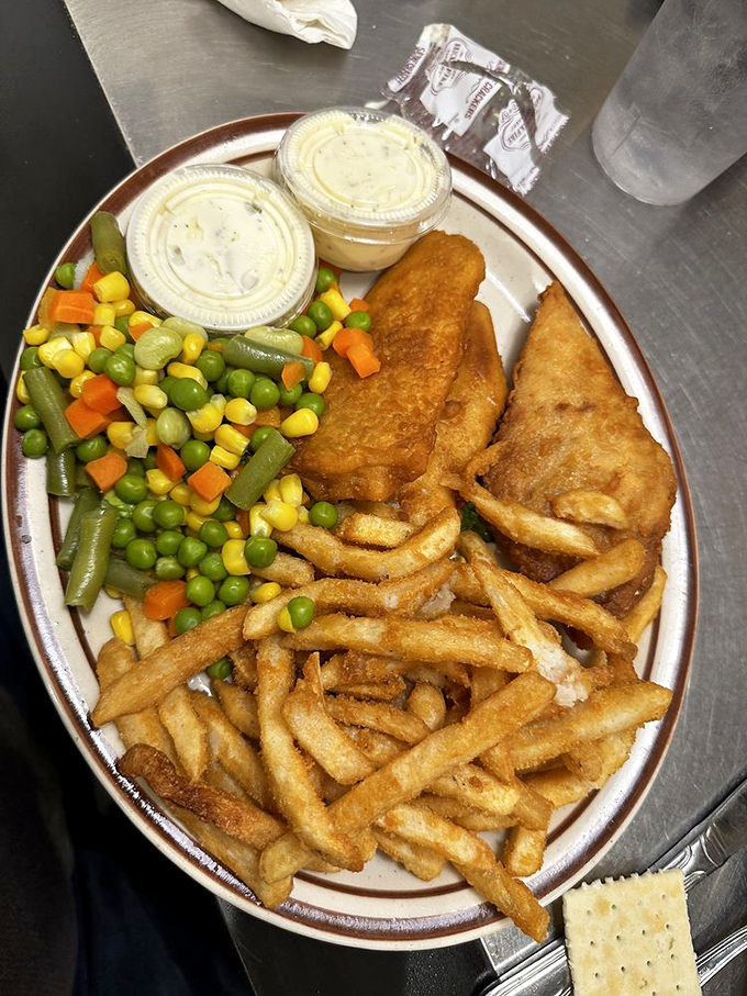 Golden-battered fish and vibrant vegetables share the spotlight on this plate. Even the tartar sauce cups look excited to be here.
