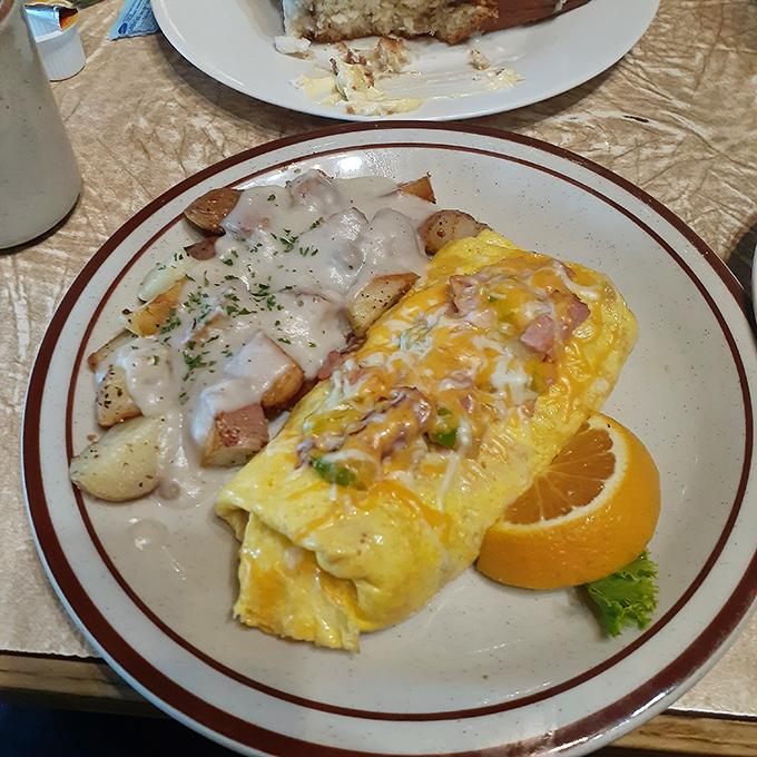 Country gravy cascades over potatoes while the omelet stands proud, a testament to the simple perfection of ham, cheese, and expert technique.