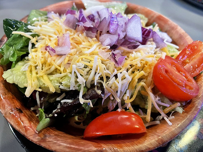 Not just a token salad &ndash; this wooden bowl holds fresh greens, vibrant tomatoes, and generous cheese that proves vegetables can have fun too.