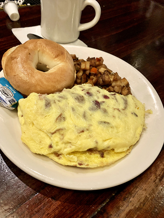 Breakfast diplomacy at its finest &ndash; a fluffy omelet stuffed with savory goodness, served with home fries and a bagel for proper morning negotiations.