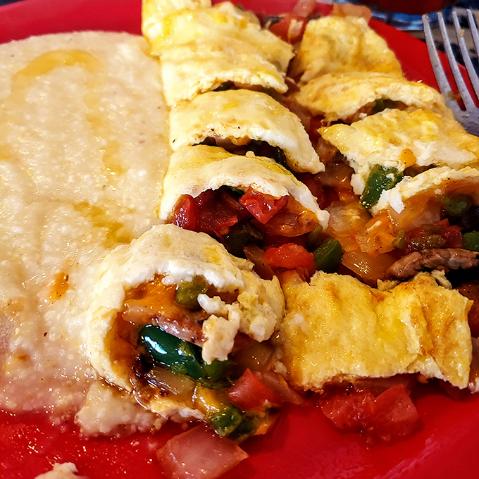 This isn't just an omelet; it's a colorful parade of vegetables tucked into a fluffy egg blanket beside creamy grits.