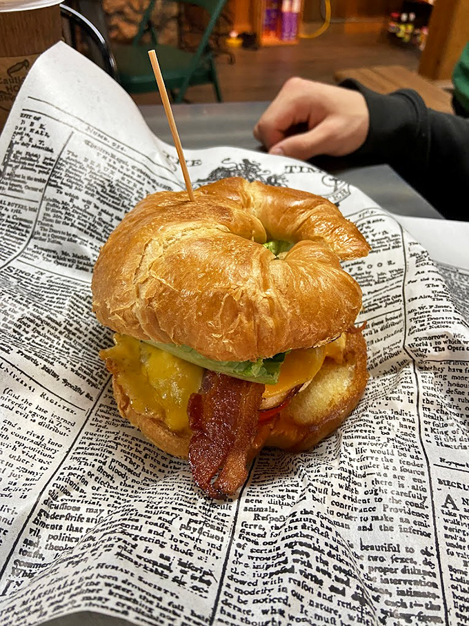 Behold breakfast perfection: a golden croissant cradling bacon, egg, and cheese. Like morning sunshine on a newspaper-lined plate.