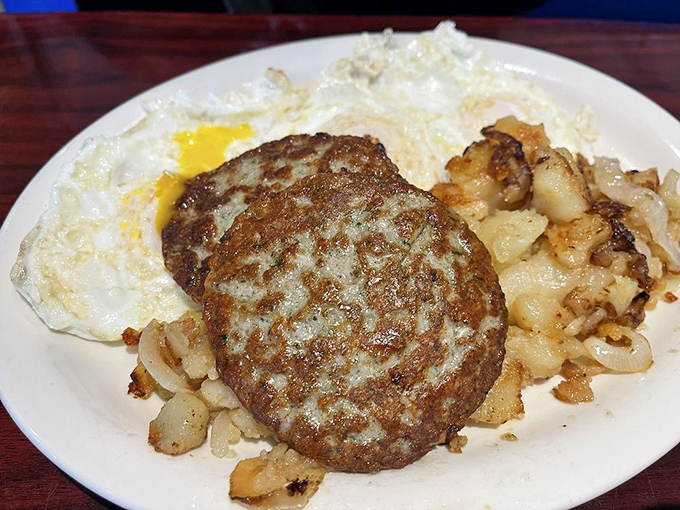 The sausage patty sits like a champion boxer between rounds, flanked by loyal cornermen: golden potatoes and eggs awaiting your fork's first jab.