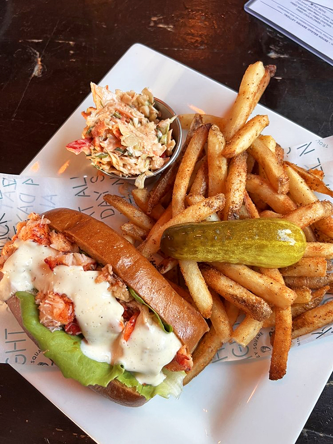 A lobster roll that's dressed to impress, with a side of perfectly golden fries. That pickle isn't just garnish—it's the acid counterpoint to buttery bliss.